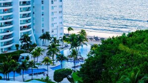 Um hotel com piscina, palmeiras e vista para o oceano.