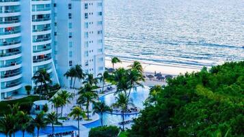 Um hotel com piscina, palmeiras e vista para o oceano.