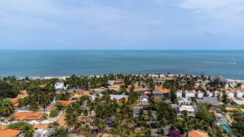 Uma vila costeira com praia, casas de telhados de palha e palmeiras.