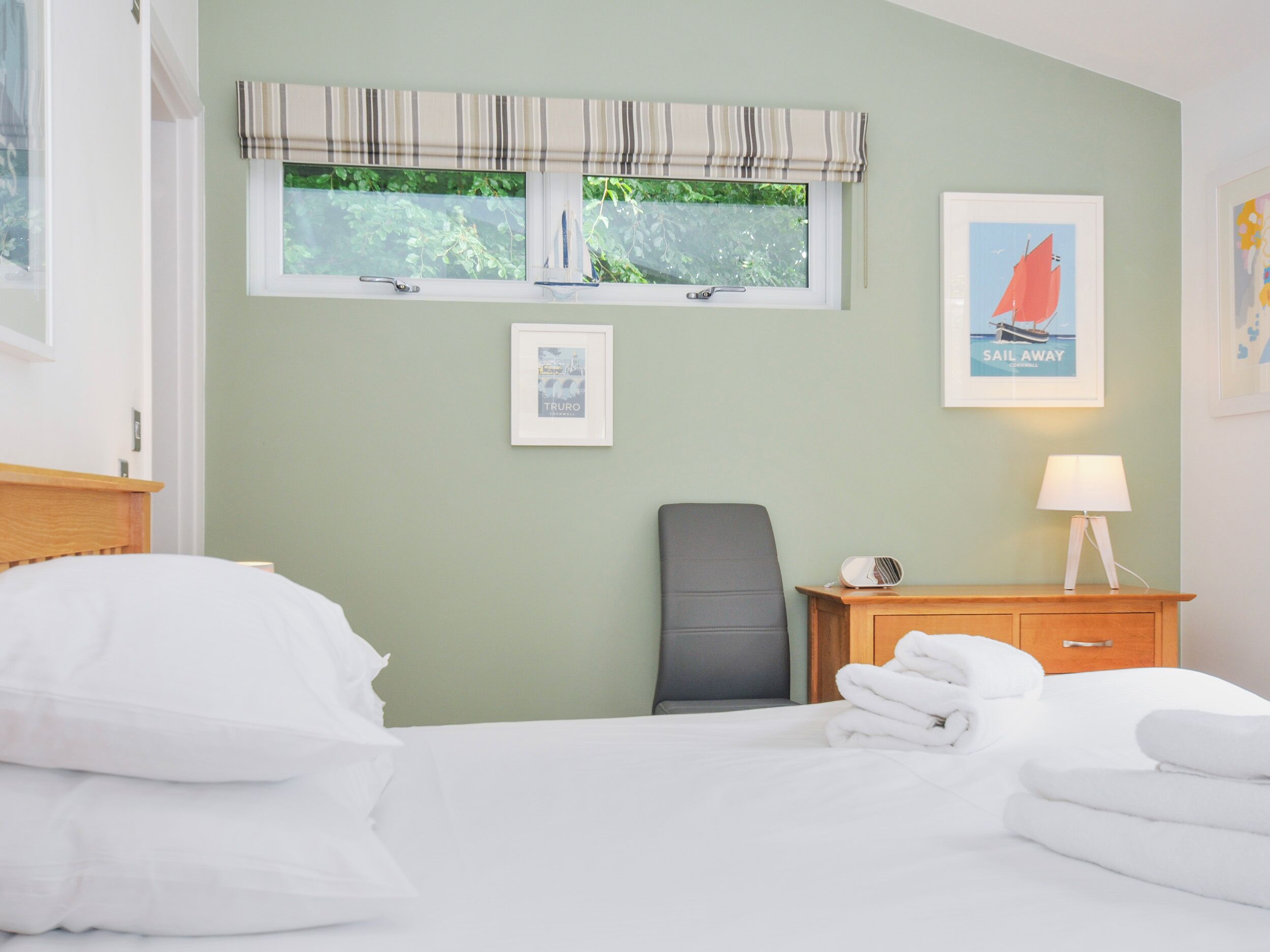 Quarto de hotel com cama, uma cadeira, mesa de cabeceira com abajur e janela com cortinas.