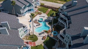Um complexo residencial com vários edifícios de dois andares, piscina central e áreas verdes ao redor.
