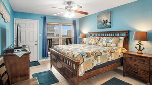 Quarto com cama, mesas de cabeceira de madeira, escrivaninha, ventilador de teto e janela com persianas.