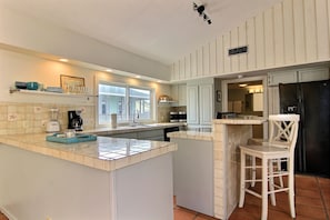 Cozinha com armários brancos, painel de azulejos, uma cafeteira e um liquidificador no balcão.