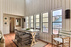 Uma área de refeições com cadeiras de vime e uma mesa, janelas amplas e vista para o exterior.
