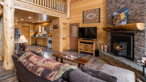 Interior de uma cabana de tronco com sala de estar, cozinha e lareira.