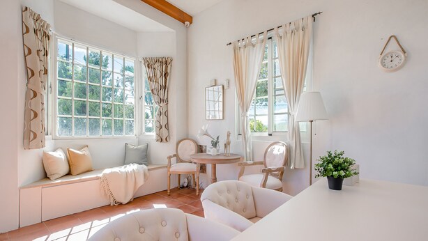 Um quarto aconchegante com sofá, cadeiras, uma mesinha e um vaso de planta.
