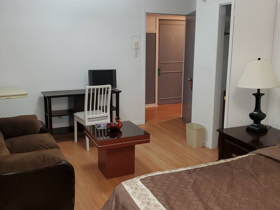 Quarto de hotel com cama, duas poltronas, uma mesinha com objeto decorativo, escrivaninha com cadeira, luminária e guarda-roupa.