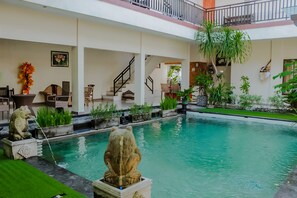 Uma área de piscina com uma estátua de sapo, plantas internas e uma escadaria.