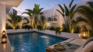 Uma área de piscina com um elemento aquático, rodeada por vegetação tropical exuberante e iluminação decorativa.
