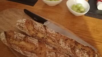 Uma mesa de madeira com um pão, uma faca e tigelas de uvas e queijo.