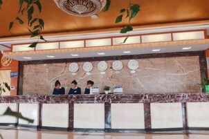 Balcão de recepção de hotel com bancada de mármore, três funcionários e um relógio de parede.