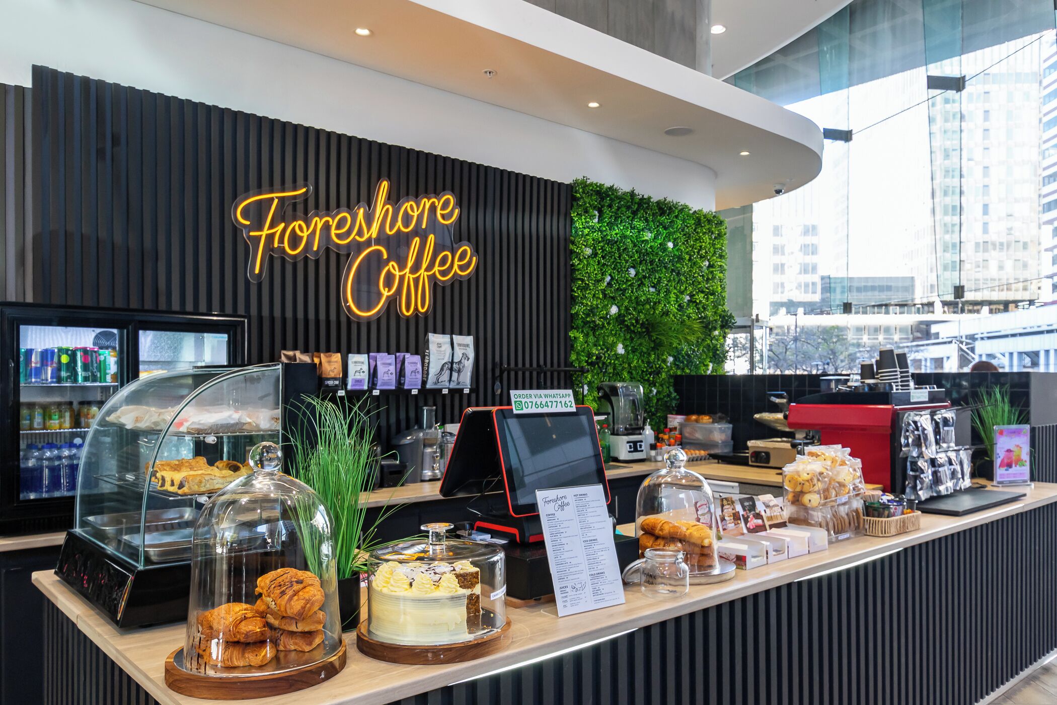 Balcão de café com um letreiro de neon, uma máquina registradora e diversos produtos de panificação expostos.