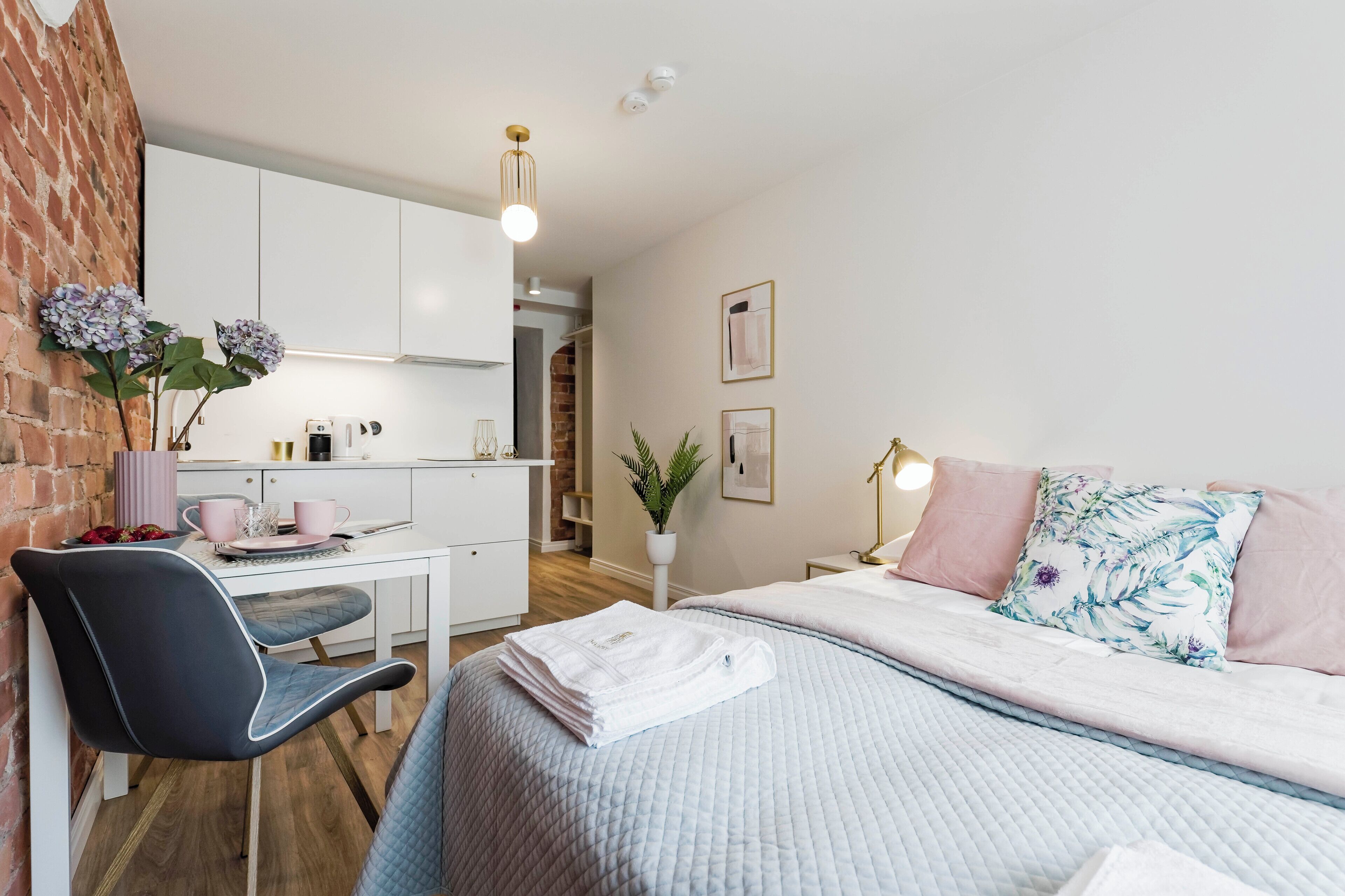 Quarto com cama, escrivaninha e cadeira. Apresenta uma parede de tijolos e teto branco.
