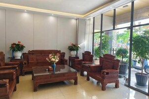 Um saguão de hotel com um conjunto de sofás, poltronas, uma mesa de centro e plantas em vasos.