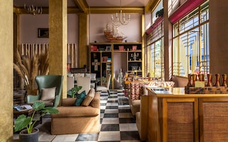Uma sala de estar ampla com piso xadrez, uma poltrona verde, um sofá e um espaço bar com pinos de boliche.