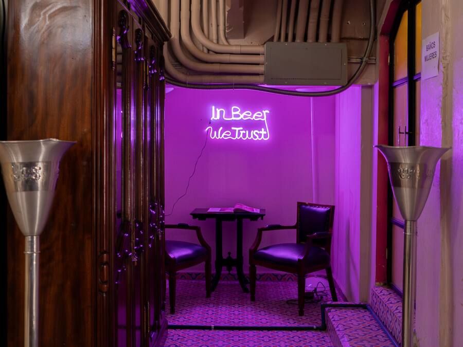 Um corredor estreito com piso de azulejos estampados, um letreiro de neon com a inscrição