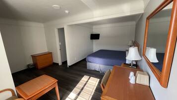 Quarto de hotel com cama, escrivaninha, penteadeira, espelho e televisão.