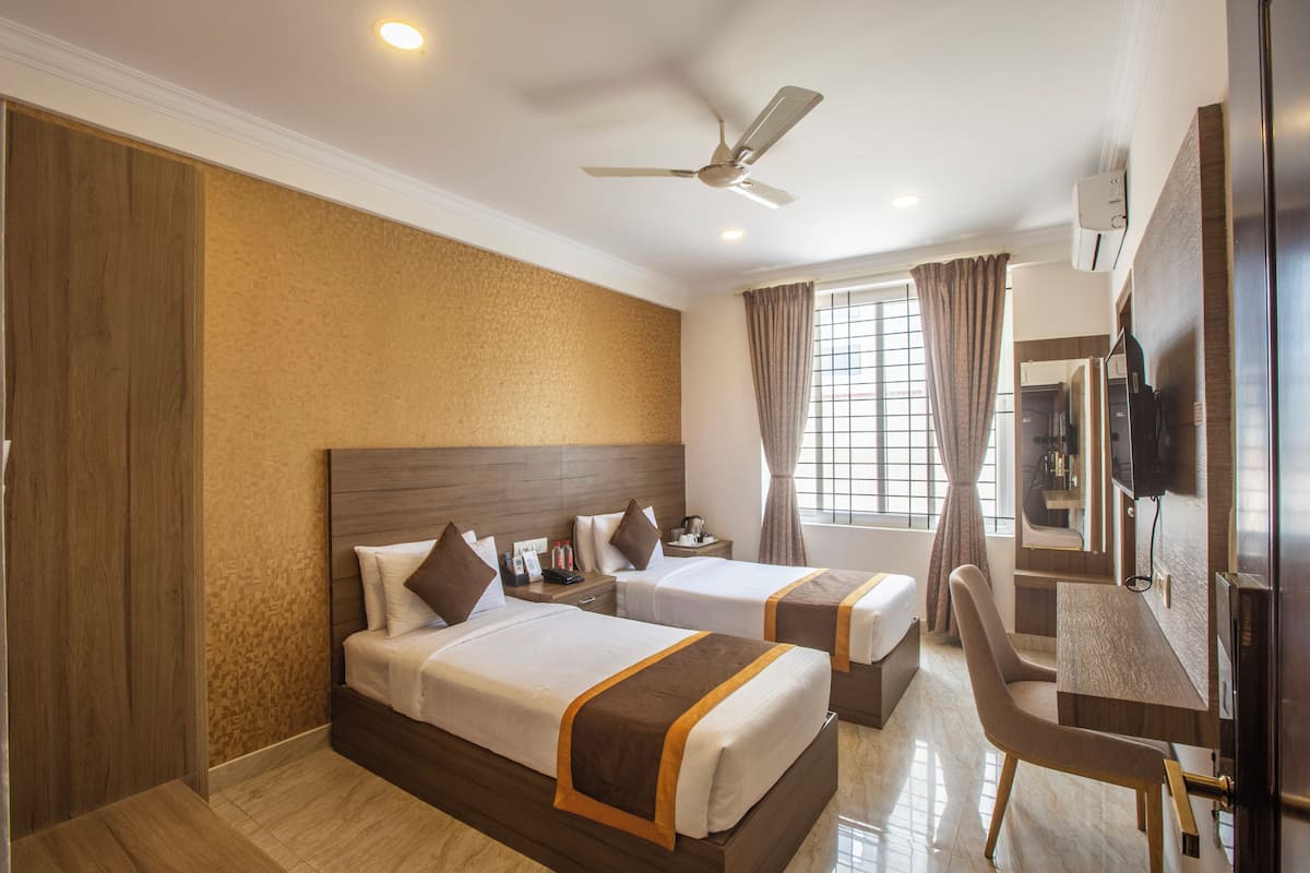 Quarto de hotel com duas camas, uma escrivaninha, uma cadeira, um ventilador de teto e uma janela com cortinas.