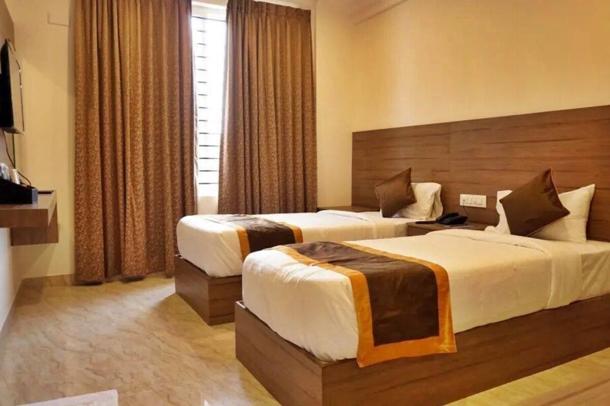 Quarto de hotel com duas camas, cabeceira de madeira, televisão de tela plana e janela com cortinas.