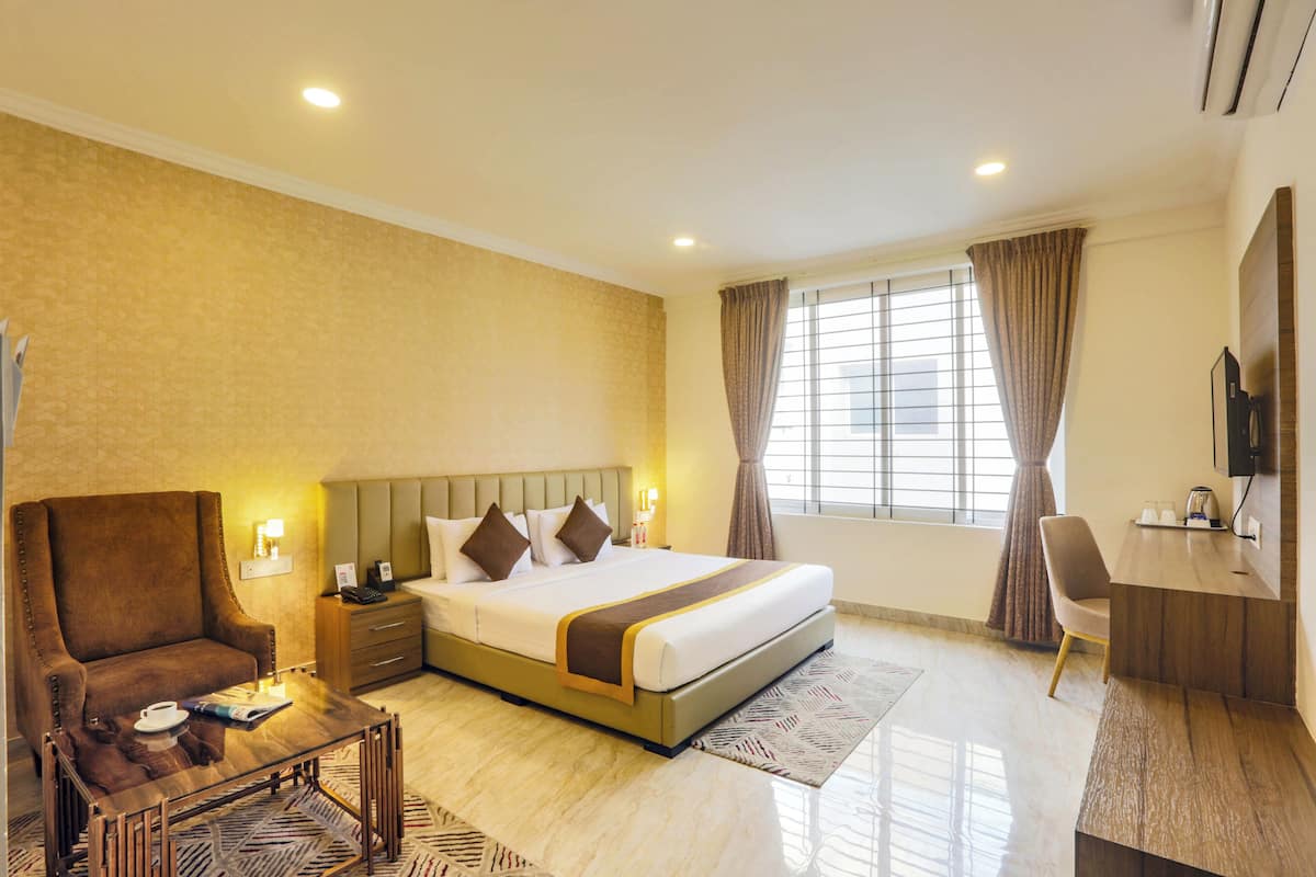 Quarto de hotel com cama, escrivaninha, cadeira, mesa de cabeceira e mesinha de centro.