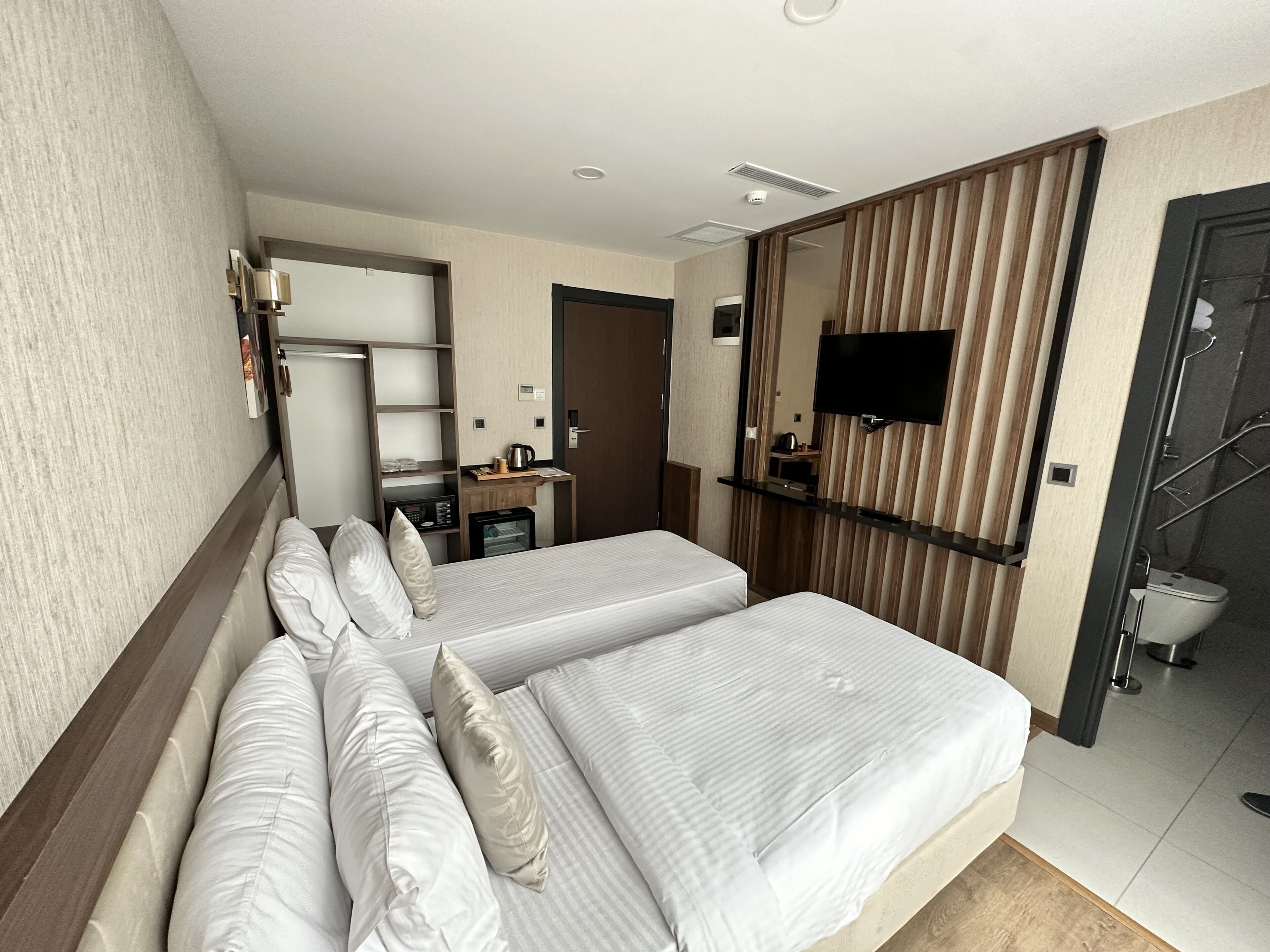 Quarto de hotel com duas camas, uma escrivaninha, televisão e banheiro.