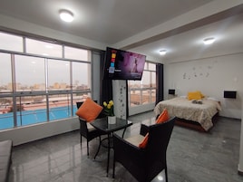 Quarto de hotel com cama, televisão, mesa de jantar e cadeiras, e vista para a piscina.