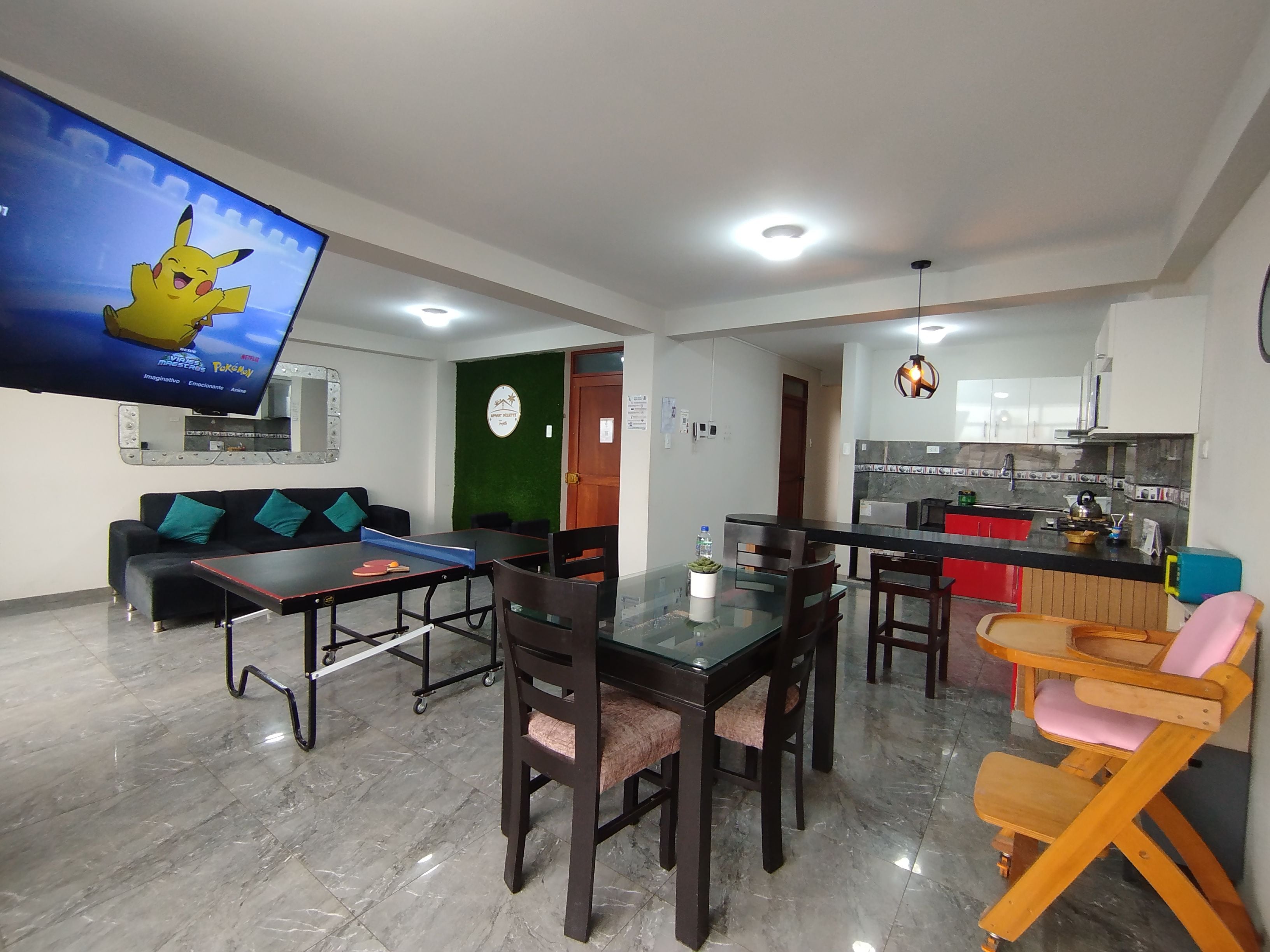 Uma sala de estar moderna com televisão de tela plana, sofá, mesa de jantar com cadeiras e cozinha.