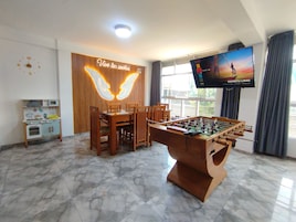 Quarto com mesa de pebolim, televisão, área de cozinha e parede com iluminação decorativa.