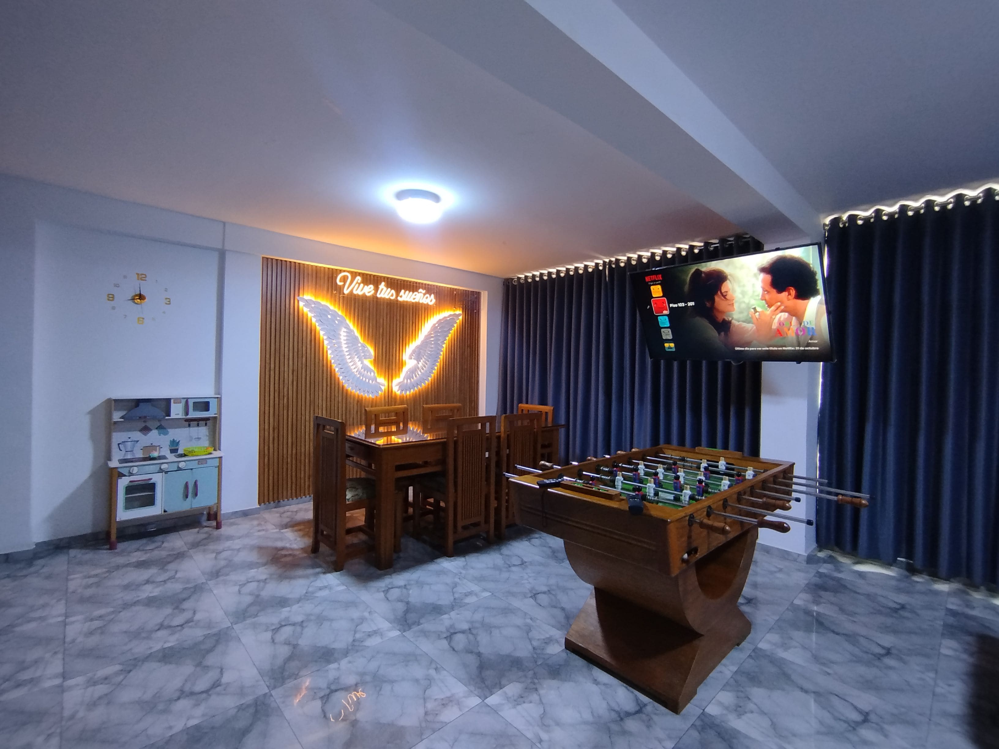 Quarto com mesa de pebolim, televisão e luminária decorativa na parede.