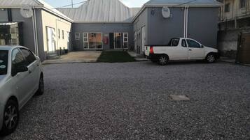 Uma entrada de cascalho leva a um edifício com fachada cinzenta e um carro branco estacionado em frente.