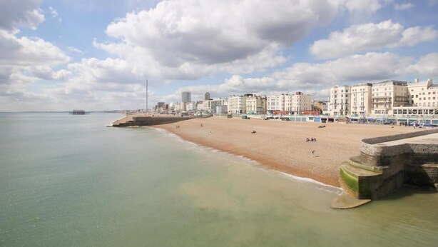 Paisagem costeira com praia arenosa, edifícios e céu claro.