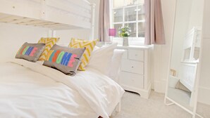 Quarto com beliches, mesa de cabeceira com abajur, espelho e janela com cortinas.