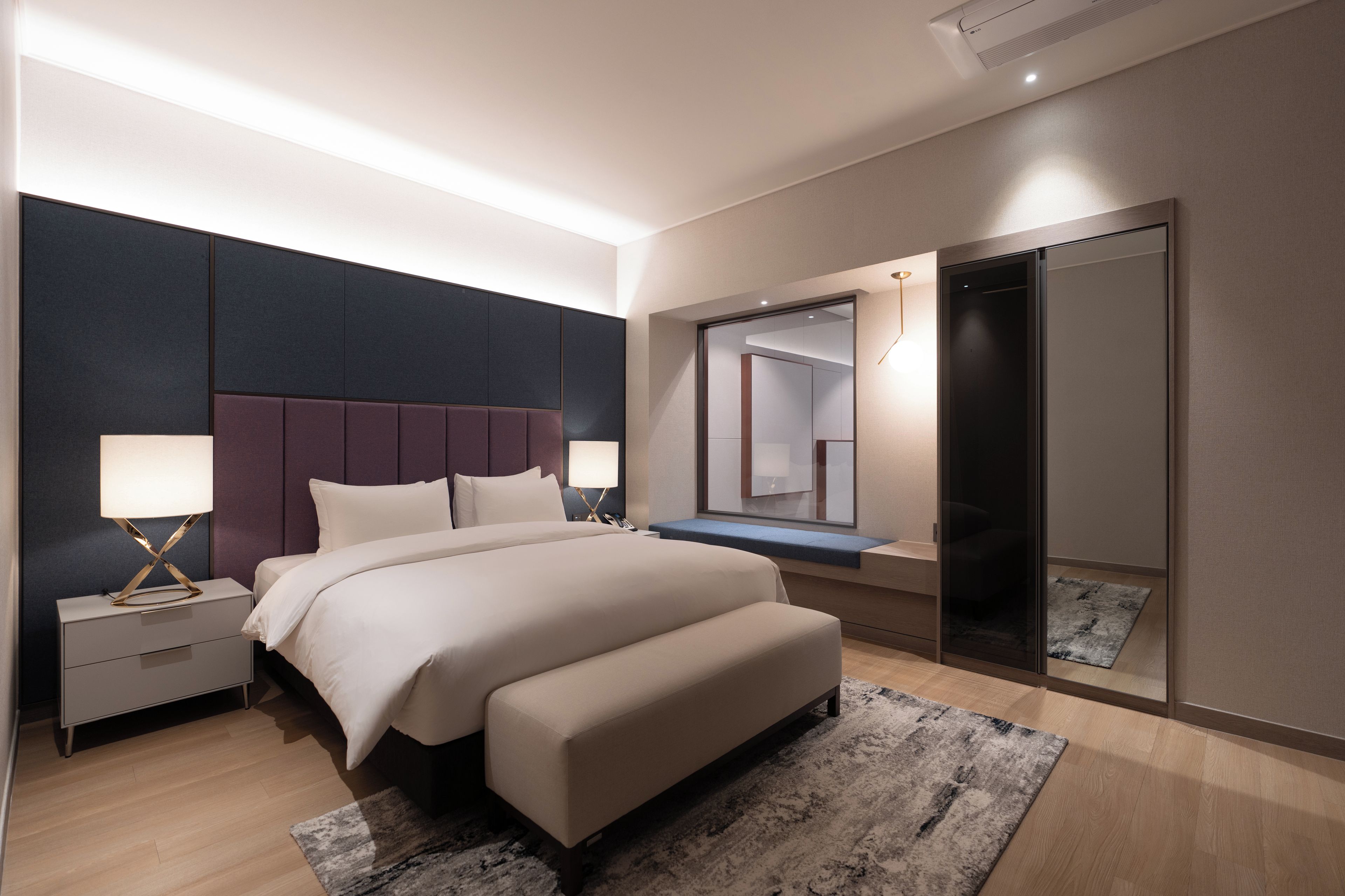 Quarto de hotel moderno com uma cama grande, mesas de cabeceira, escrivaninha, cadeira, espelho e guarda-roupa.