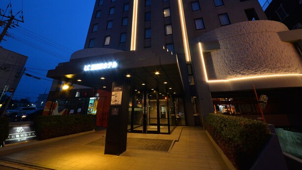 Entrada de hotel com porta de vidro, letreiros iluminados e um caminho de ladrilhos.