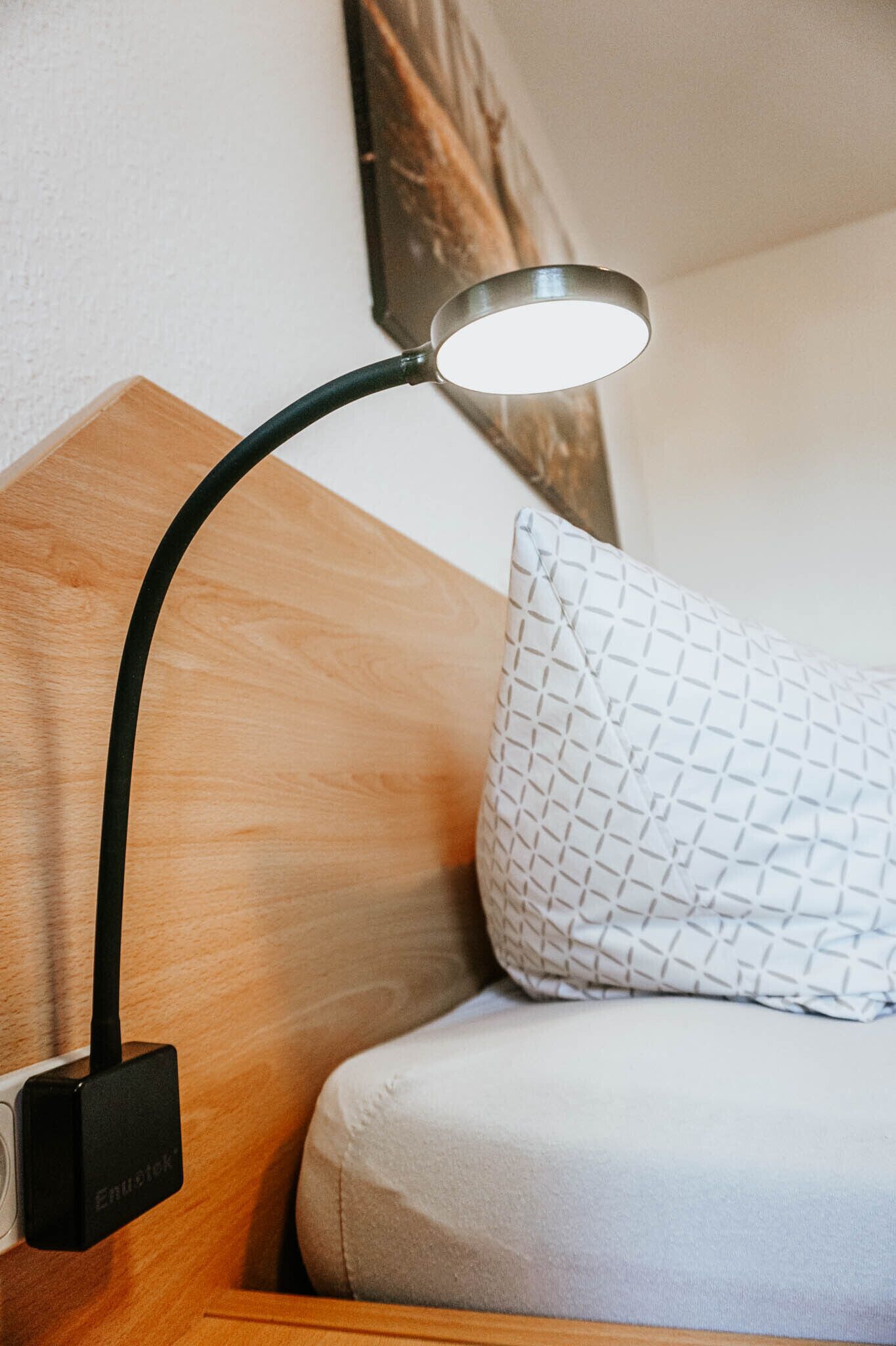Uma mesa de cabeceira moderna com uma luminária preta, um travesseiro branco e uma cabeceira de madeira.