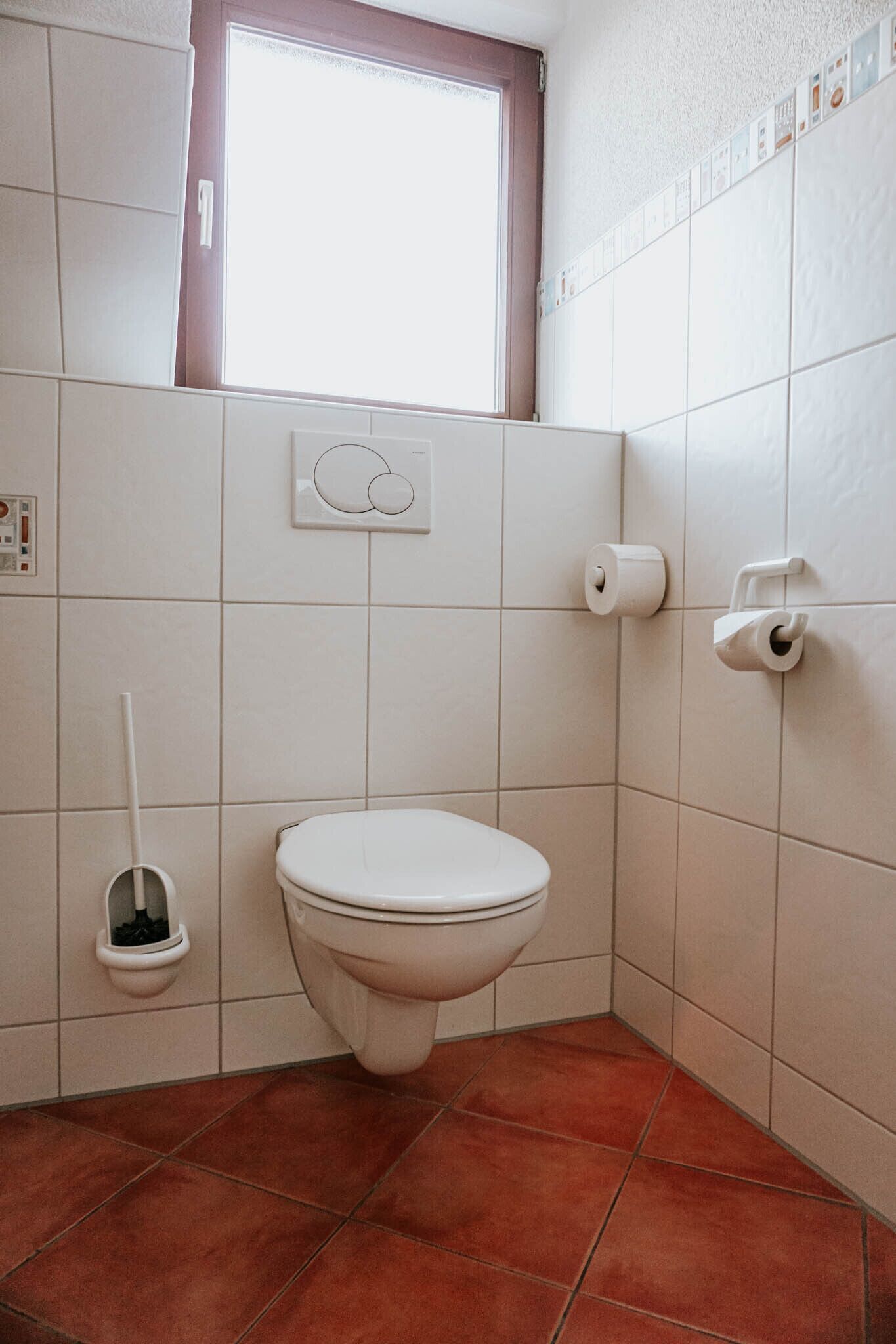 Casa de banho com sanita, janela e barra de descarga fixada na parede.