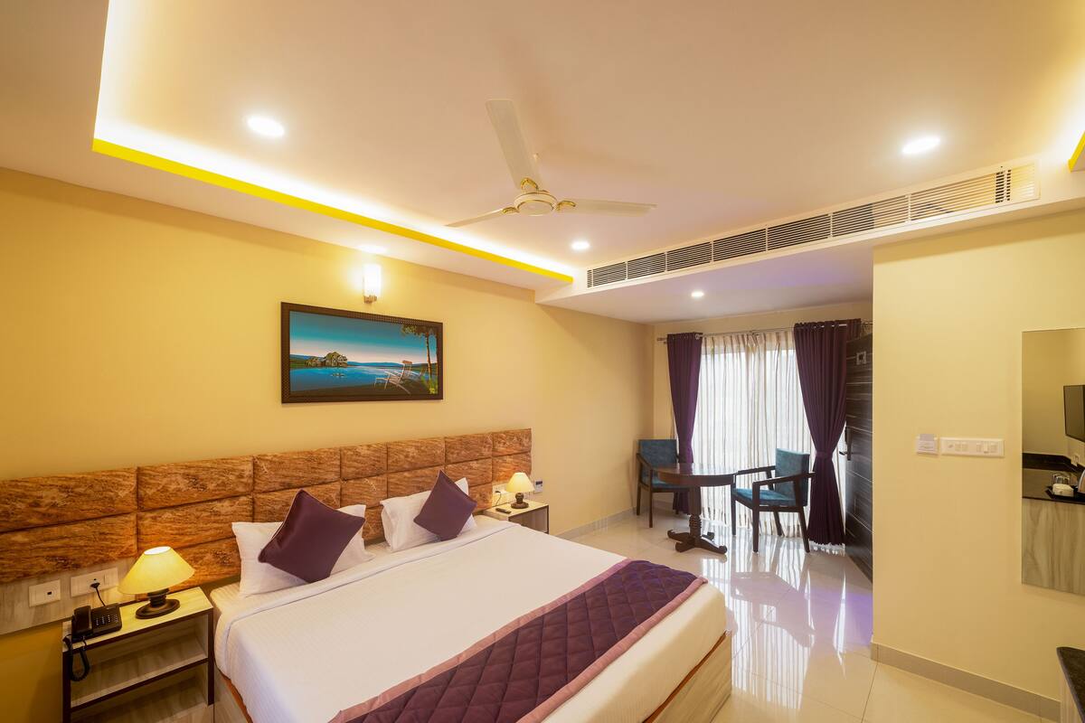 Quarto de hotel com uma cama grande, uma escrivaninha, uma cadeira, um ventilador de teto e um quadro na parede.