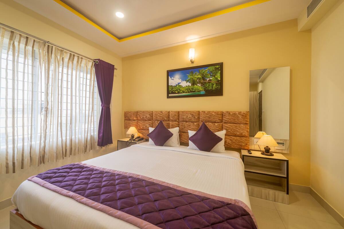 Quarto de hotel com uma cama grande, cabeceira com design texturizado, mesa de cabeceira com abajur e um quadro na parede.