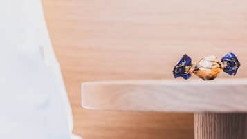 Visão nítida de uma mesa de cabeceira de madeira com tampo de vidro transparente, um cobreleiro branco e um travesseiro branco visível apenas parcialmente.