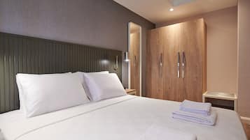 Quarto de hotel moderno com uma cama grande, um guarda-roupa de madeira e uma mesinha de cabeceira.