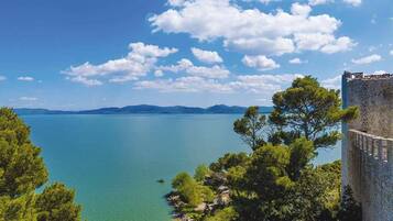 Uma torre de pedra histórica com vista para um lago tranquilo, montanhas ao longe e céus límpidos.