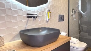 Um banheiro moderno com uma pia grande sobreposta, um móvel de madeira, um box de vidro e um revestimento de azulejos brancos.