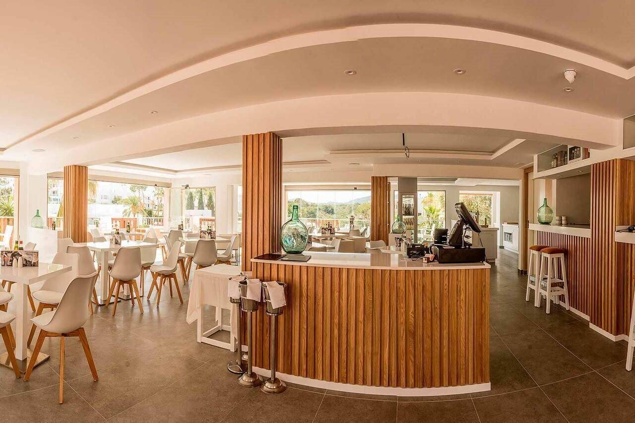 Um hall de hotel moderno com uma recepção central, áreas de estar e grandes janelas com vista para o exterior.