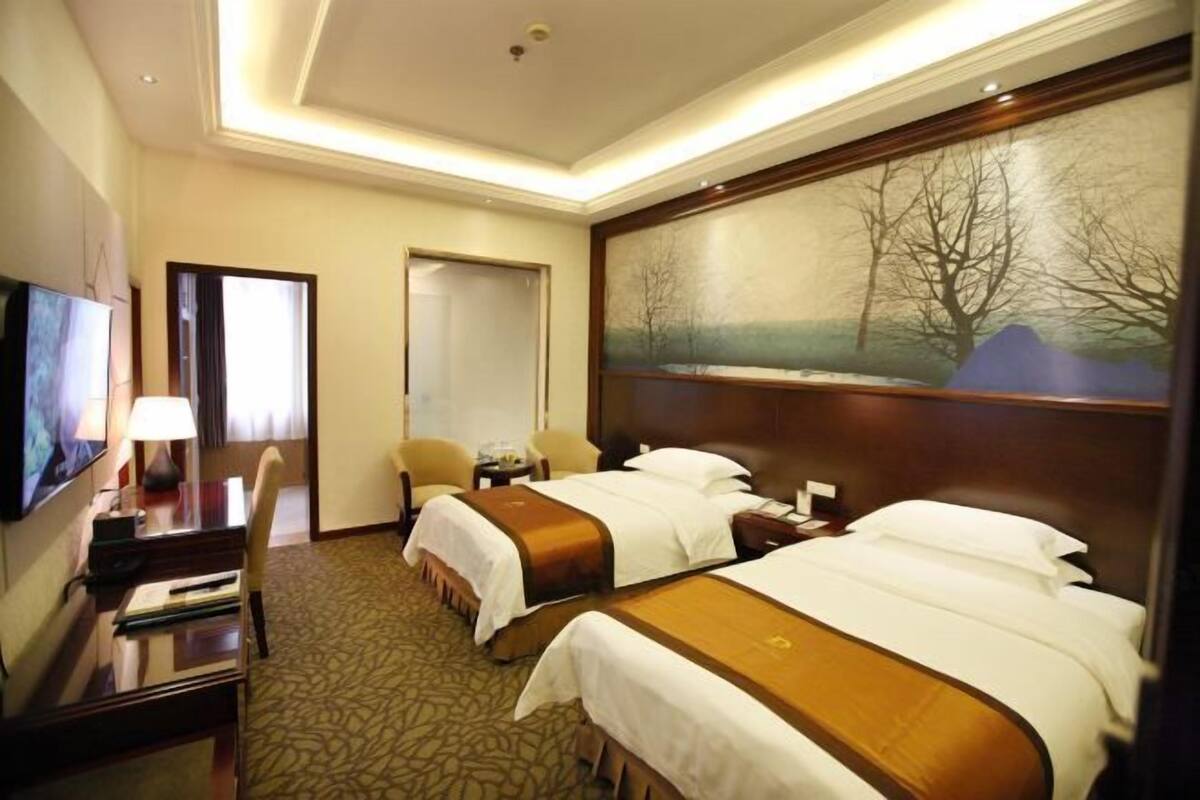 Quarto de hotel com duas camas, uma mesa, uma televisão e um quadro na parede.