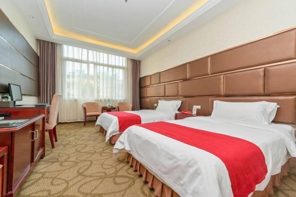 Quarto de hotel com duas camas, uma escrivaninha, uma cadeira e uma televisão.