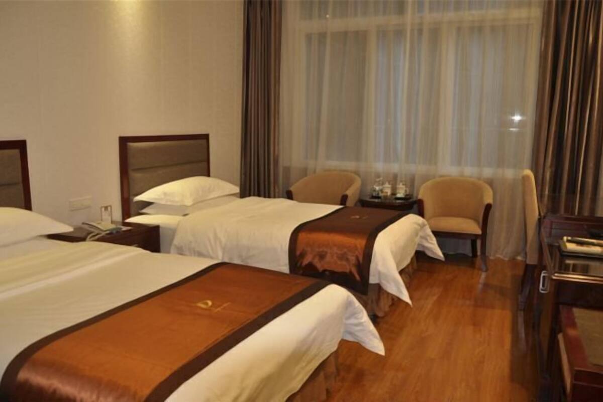 Quarto de hotel com três camas, piso de madeira e uma janela grande com cortinas.