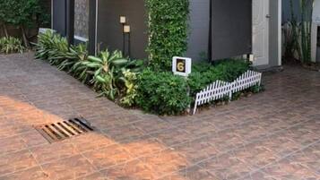 Um imóvel residencial com um alpendre coberto, um pequeno jardim com diversas plantas e uma cerca branca de piquete.