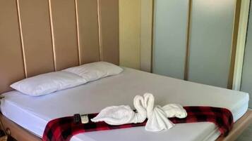 Cama bem arrumada com lençóis brancos e manta xadrez preta e vermelha, travesseiro branco e toalha disposta em formato de cisne.
