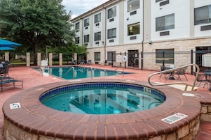 Uma área de piscina com duas piscinas, uma banheira de hidromassagem e um edifício com várias janelas e fachada de pedra.