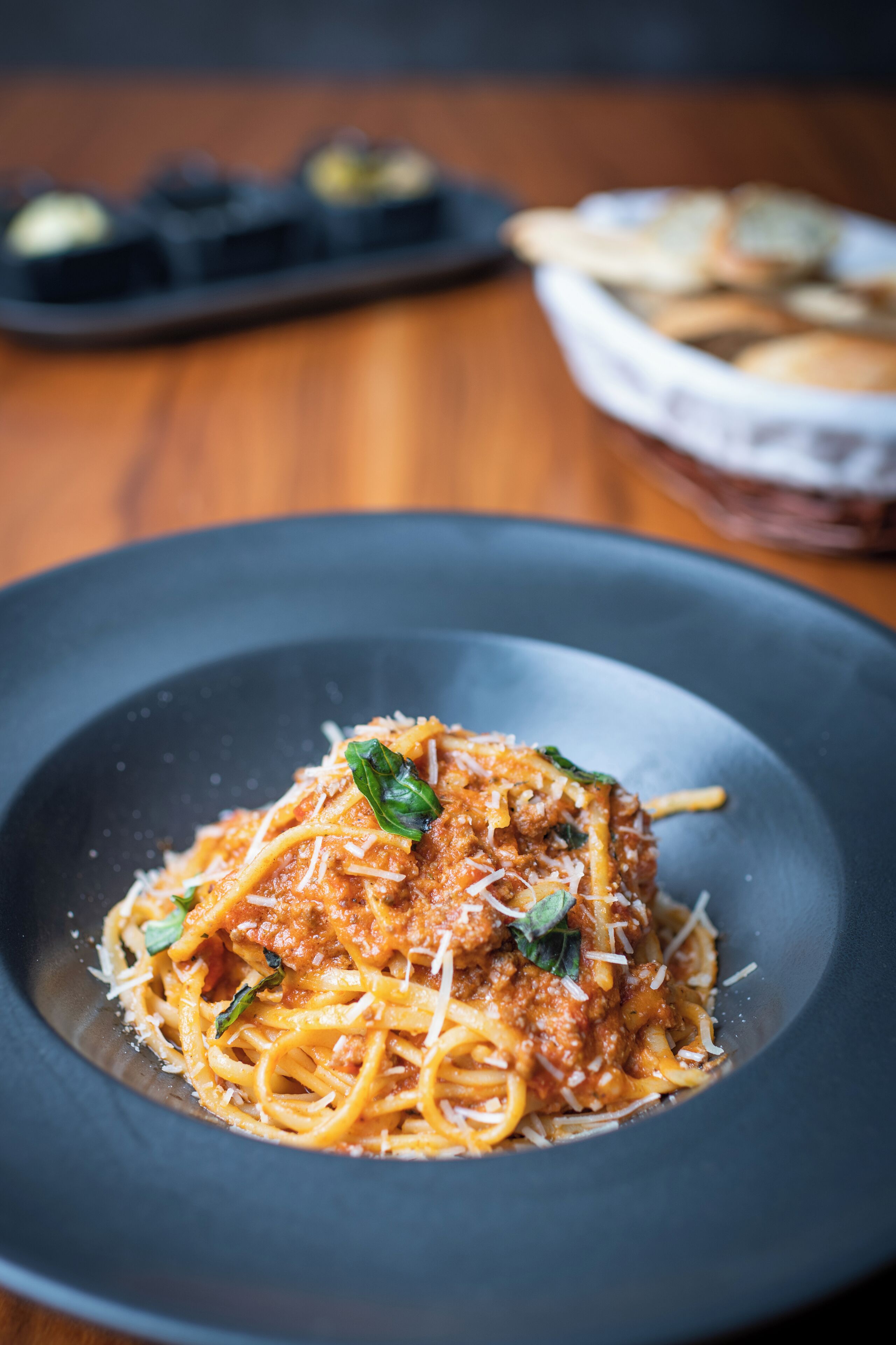 Prato de espaguete com molho de carne e queijo, decorado com manjericão, servido em prato escuro.